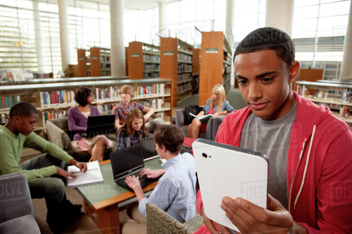 African American student on digital tablet reading with classmates ...