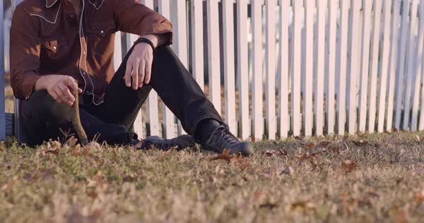 Man sitting on the ground leaning up against a white picket fence ...