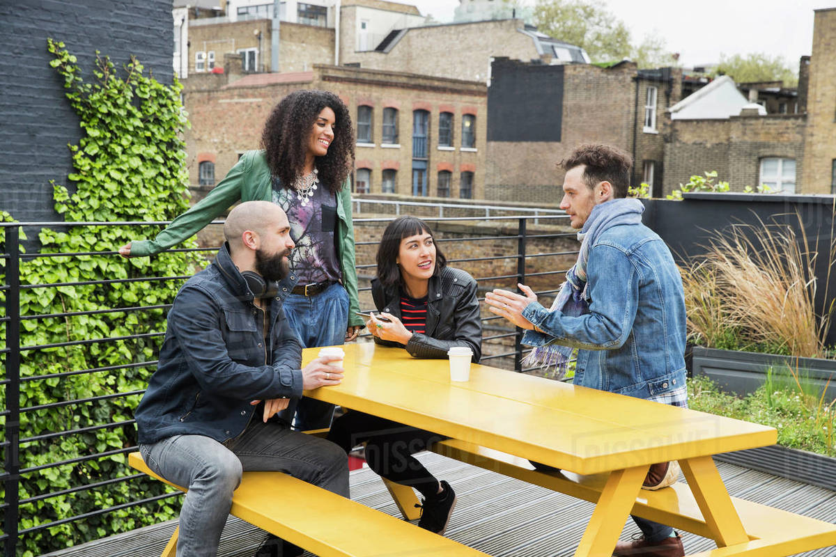 Group of friends working on tablets at outdoor patio table in co ...