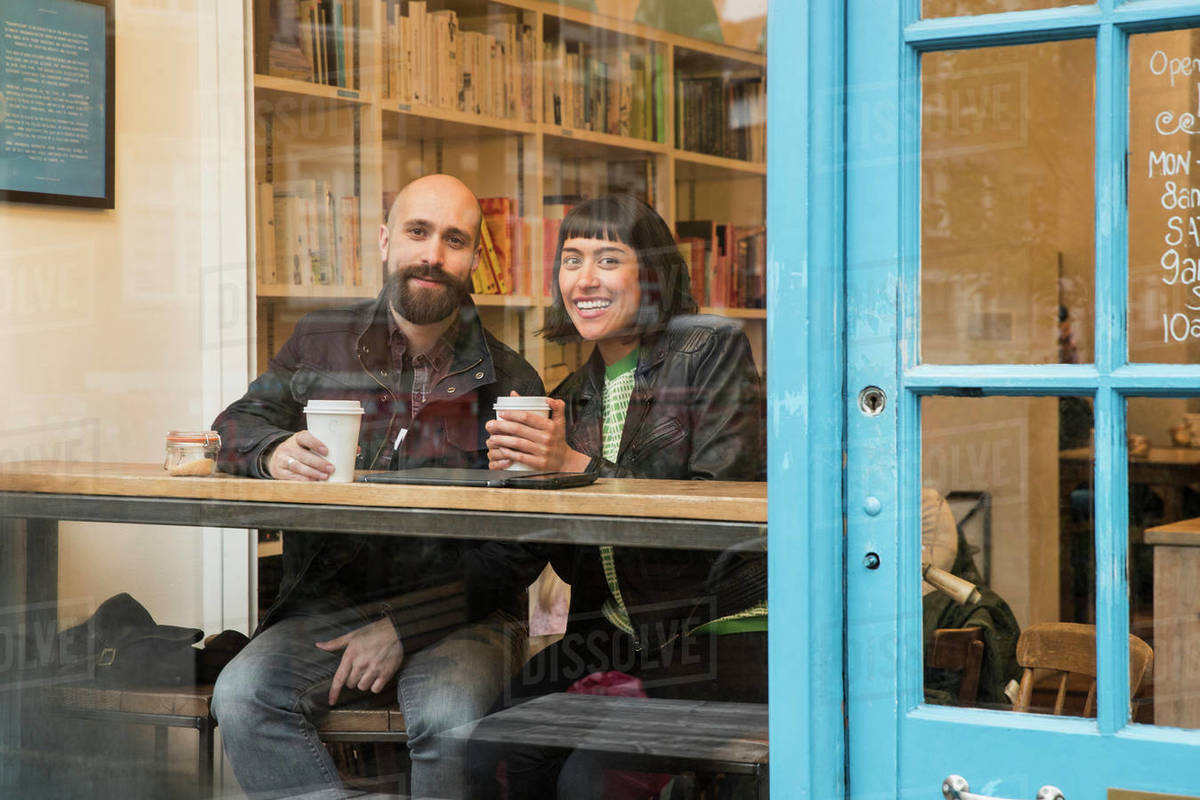 Friends sitting in window of cafe with tablet - Stock Photo - Dissolve