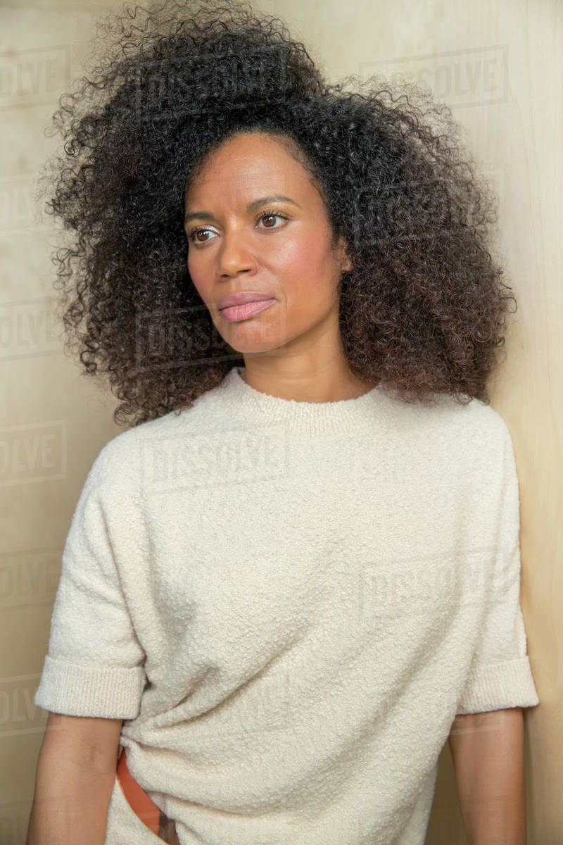 Close up portrait of a mixed race middle-aged woman leaning against a wooden wall, looking off ...