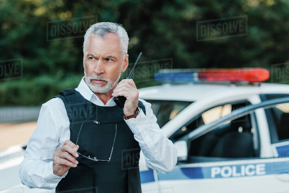 serious middle aged policeman in bulletproof vest talking on radio set ...