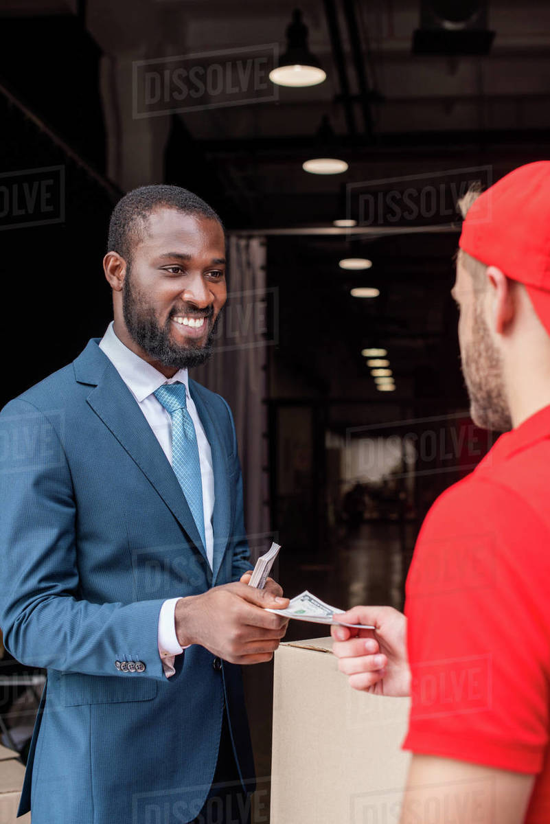 smiling african american client paying for delivery with cash - Stock ...