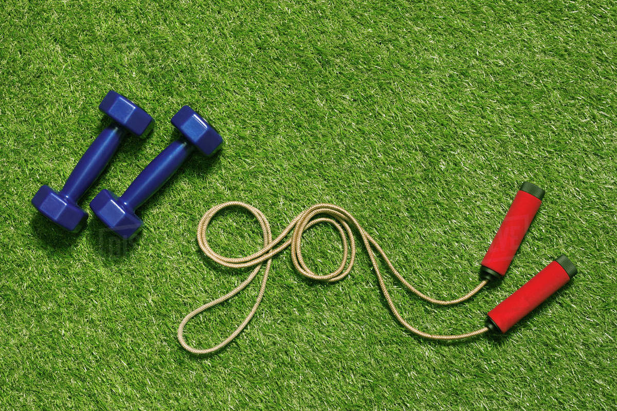 Top view of dumbbells with jump rope in shape of word go on the grass ...