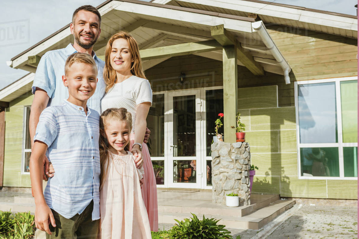 Smiling parents and children standing in front of house - Royalty-free ...
