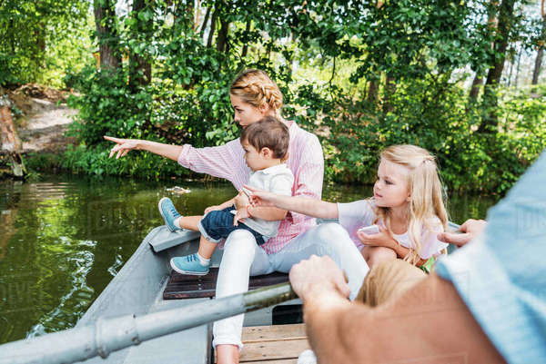 Beautiful young family riding boat on lake and pointing somewhere at ...