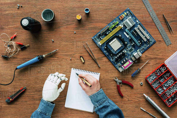 Cropped image of man with robotic hand writing in textbook by pen at ...
