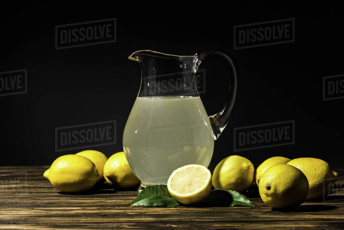 Glass jug with organic juice and yellow lemons around on wooden ...