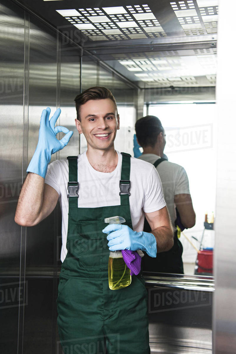 Handsome young janitor holding spray bottle with detergent and rag ...