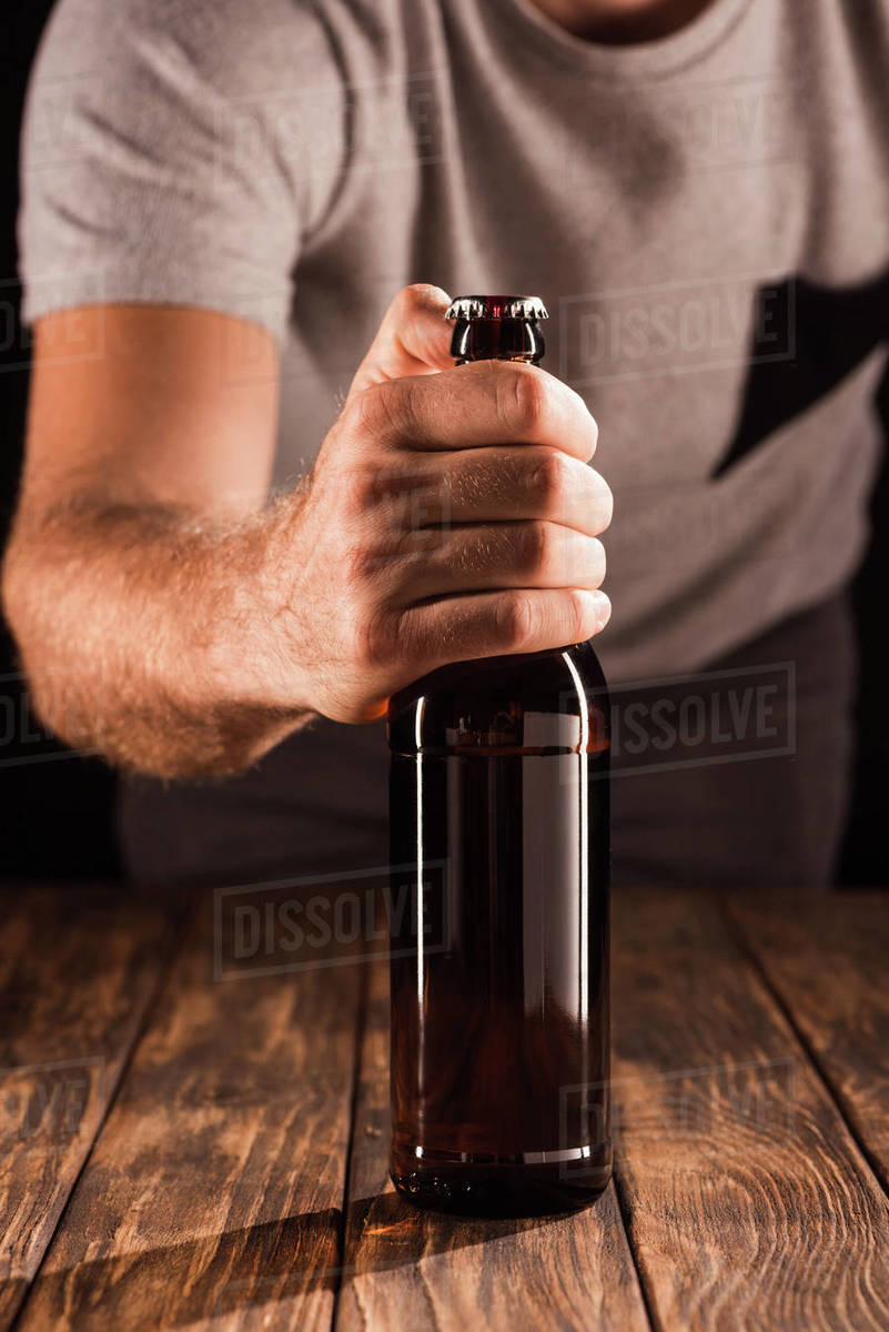 Cropped image of man opening beer bottle at wooden table - Royalty-free ...