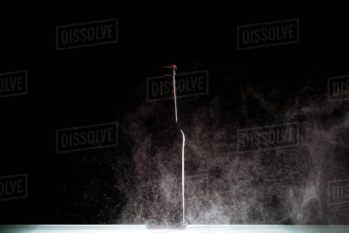 Bottle of beer with spraying water around at table on black background ...