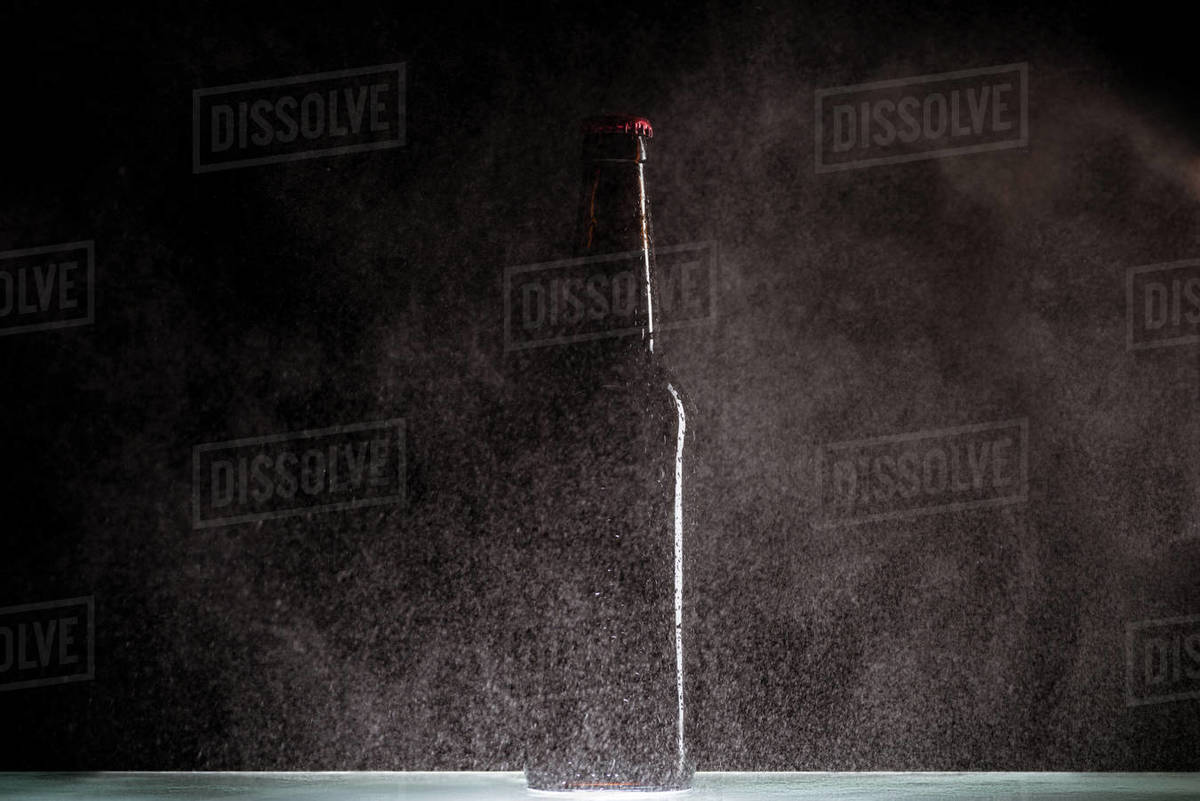 Selective focus of beer bottle with spraying water around at surface on ...