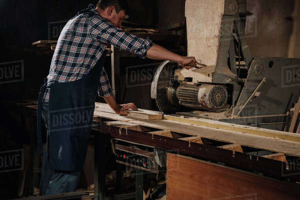 Side view of carpenter using saw at wooden workshop - Stock Photo ...