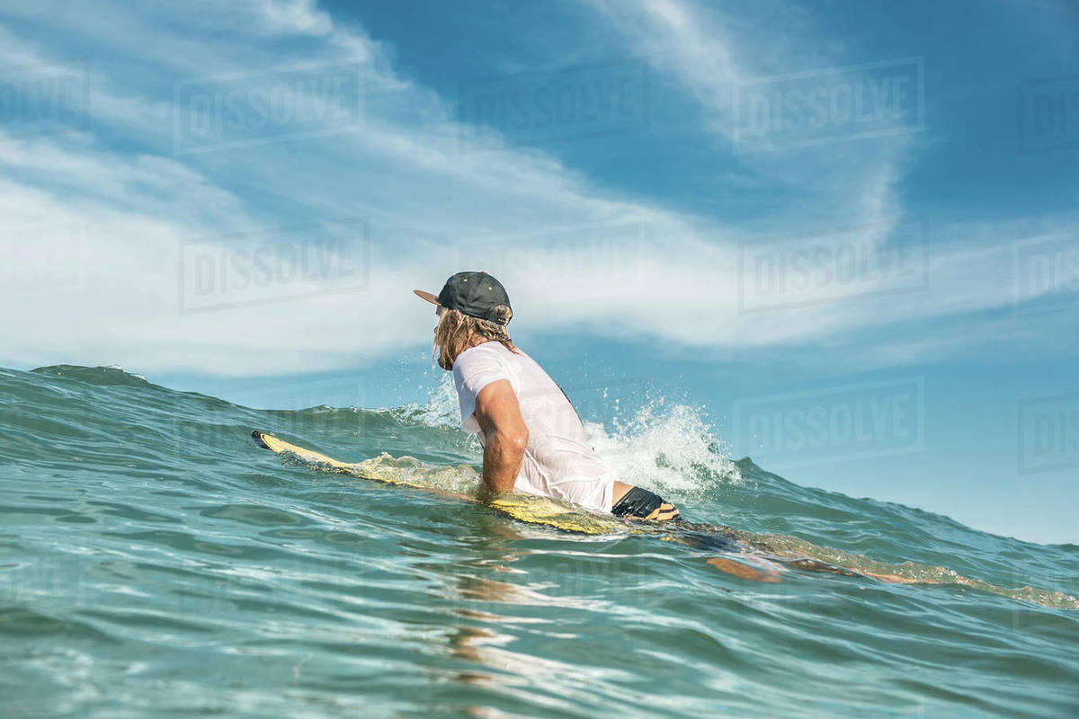 Side view of male surfer swimming on surfing board in ocean at Nusa Dua ...