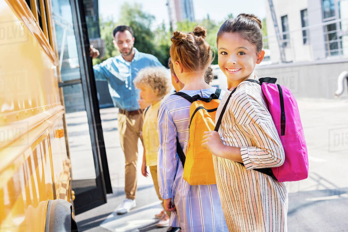 little schoolgirl entering school bus with classmates while teacher ...