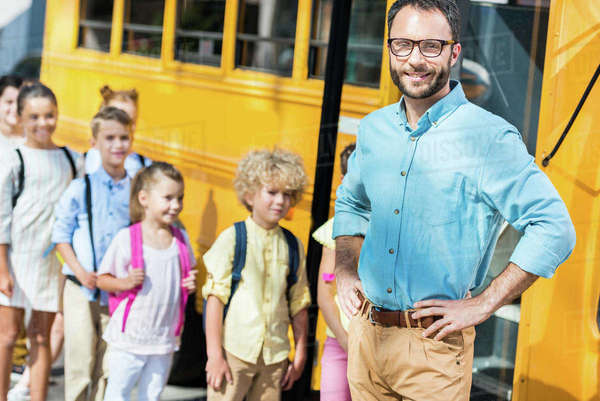 handsome male teacher looking at camera while pupils entering school ...