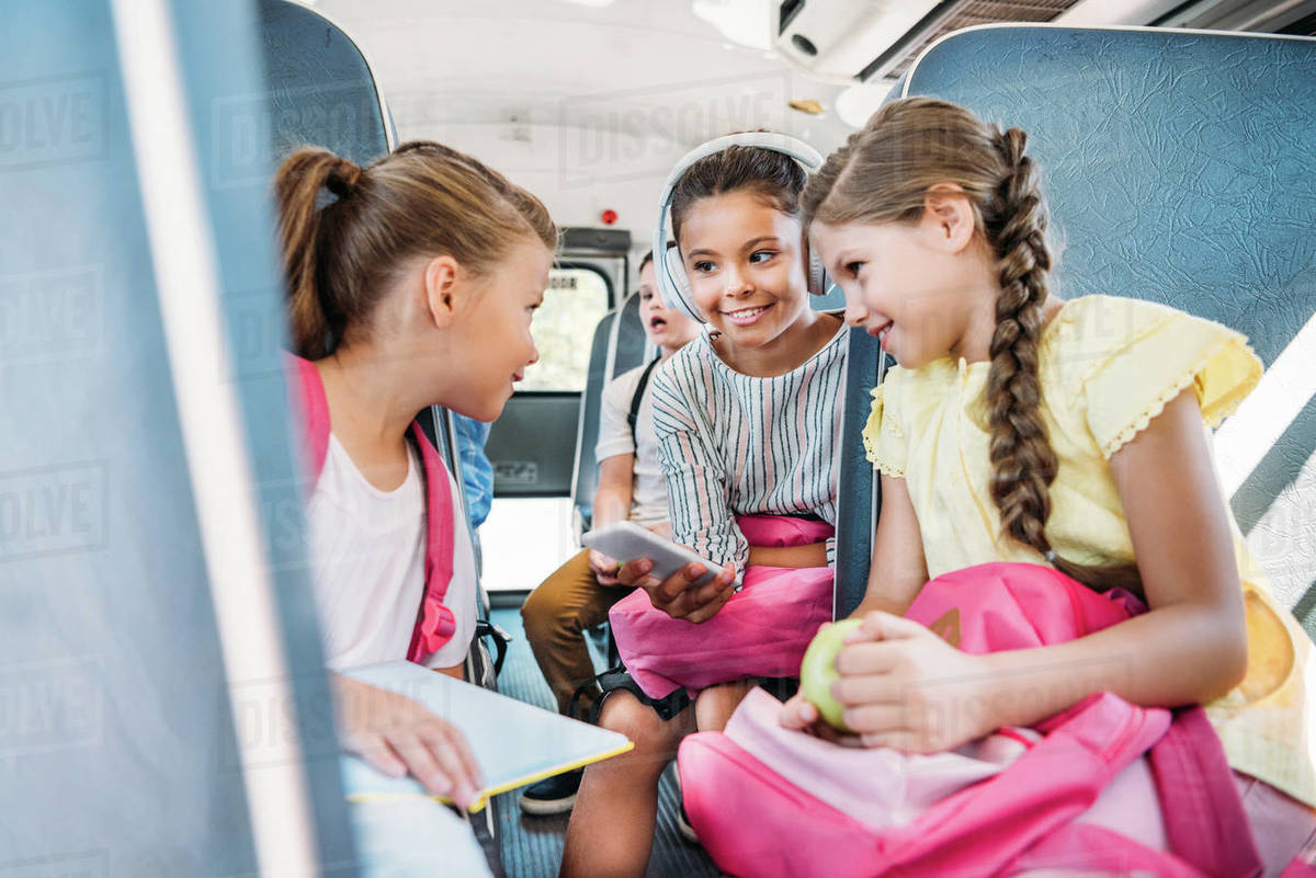 group of happy schoolgirls using smartphone together while riding on ...