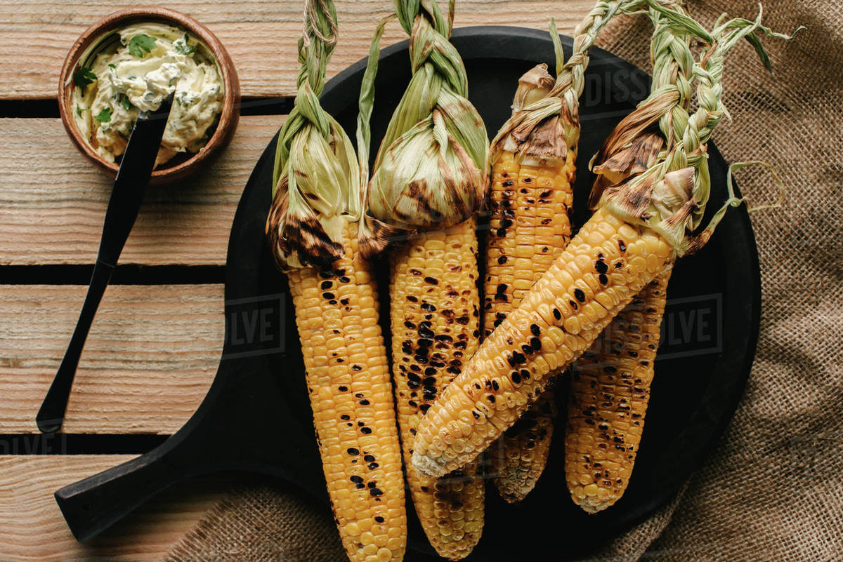 Top view of grilled corn, knife and butter with parsley on wooden table ...