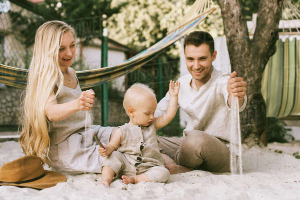 smiling parents and little son playing with sand on ground together at ...