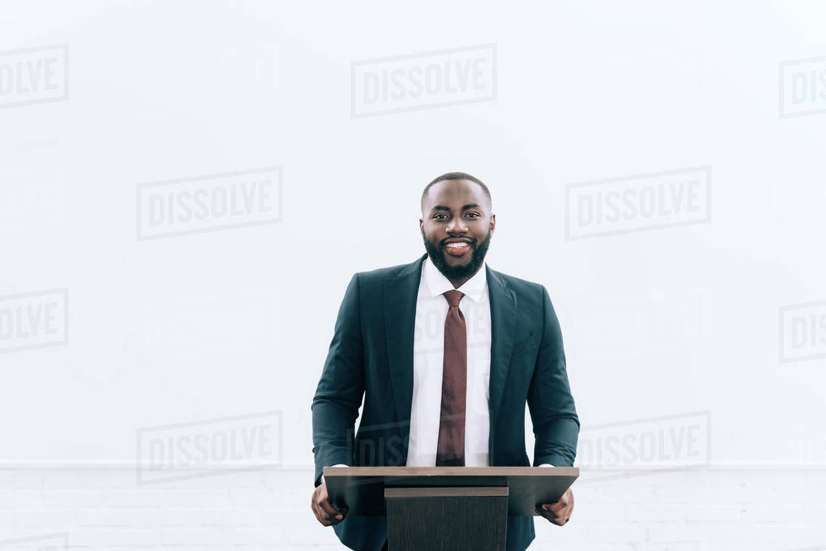 Smiling handsome african American lecturer standing at podium tribune ...