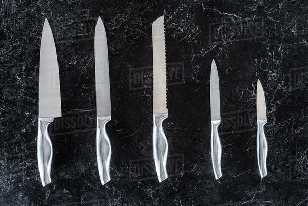 Top view of different kitchen knives arranged on black surface ...