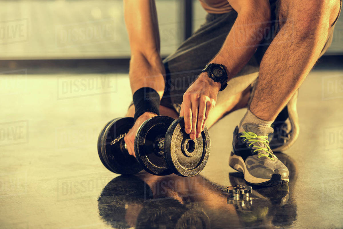 Cropped shot of sportsman putting weight on dumbbell in gym - Royalty ...