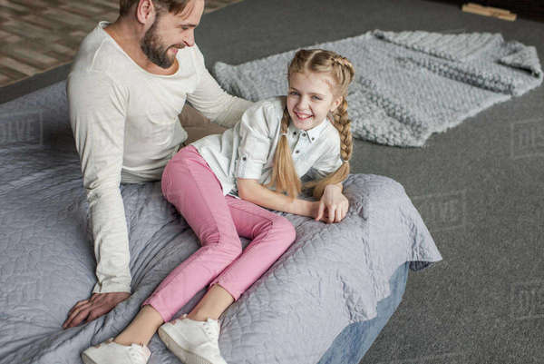 Happy adorable daughter and father sitting on bed at home - Royalty ...