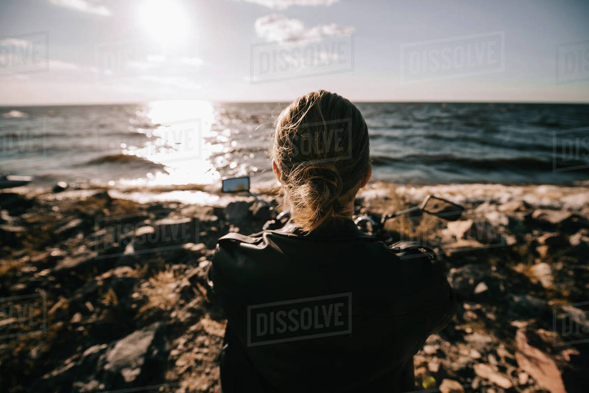 Back view of biker sitting on motorcycle and looking at sunset over the ...