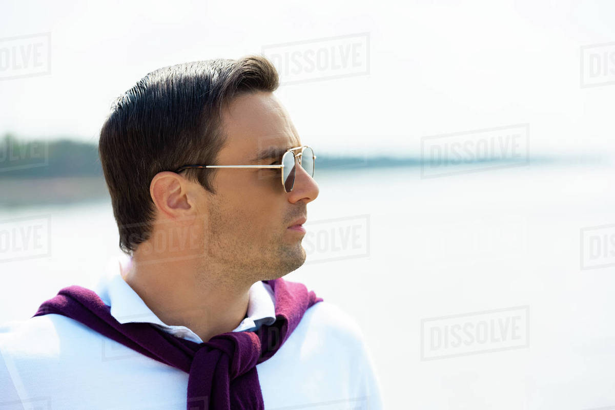 Side view of handsome man in sunglasses looking away with river on ...