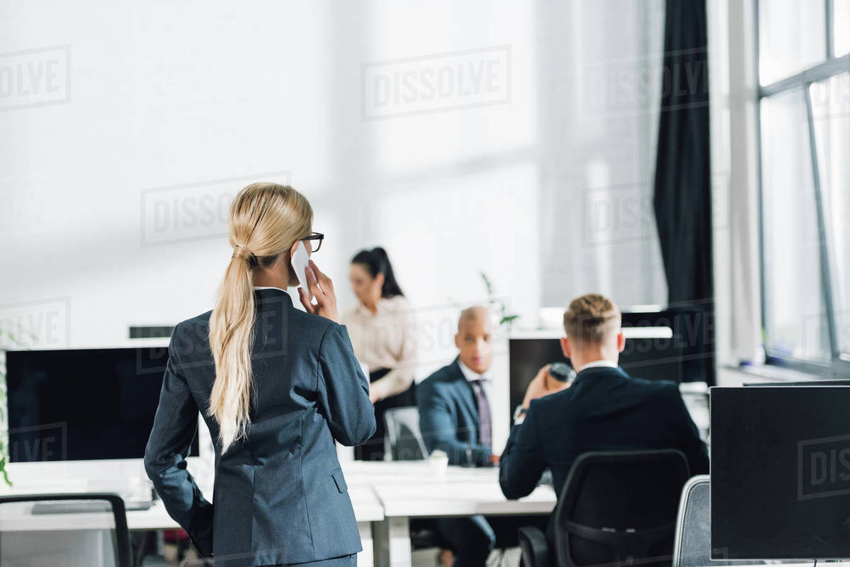 Back view of young businesswoman talking by smartphone and looking at ...