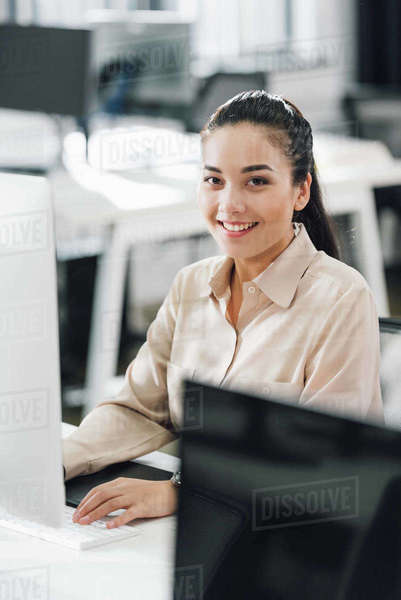 Beautiful young businesswoman using desktop computer and smiling at ...