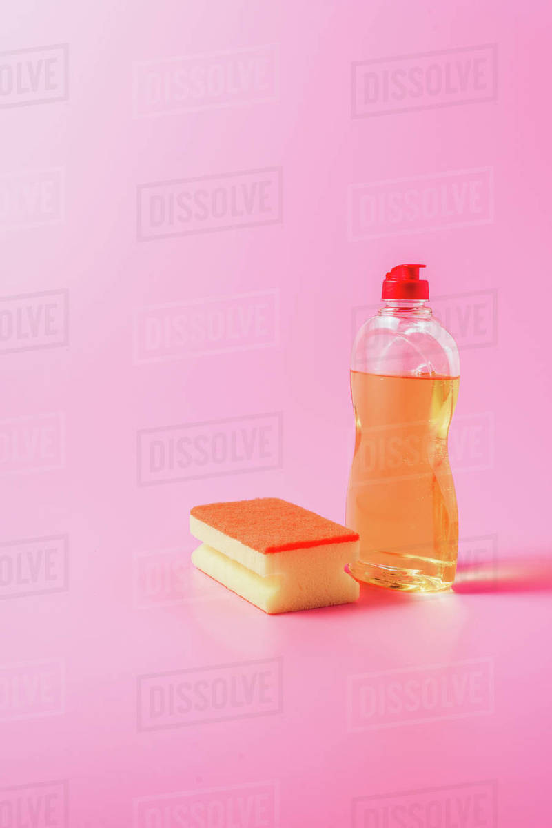 close up view of washing sponge and dishwashing liquid, pink background ...