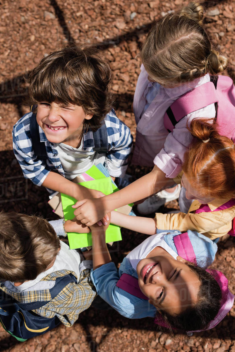 overhead view of adorable multiethnic kids stacking hands above books ...