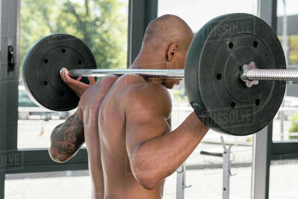 back view of muscular young sportsman lifting barbell in gym - Royalty ...