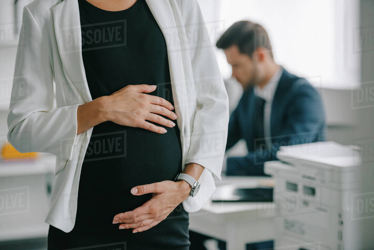 Partial view of pregnant businesswoman and colleague at workplace in ...