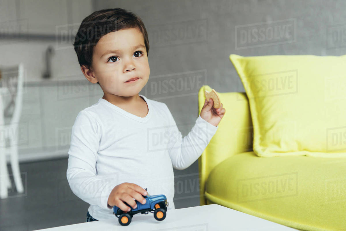 Adorable boy playing with toy car and eating cookie - Royalty-free ...
