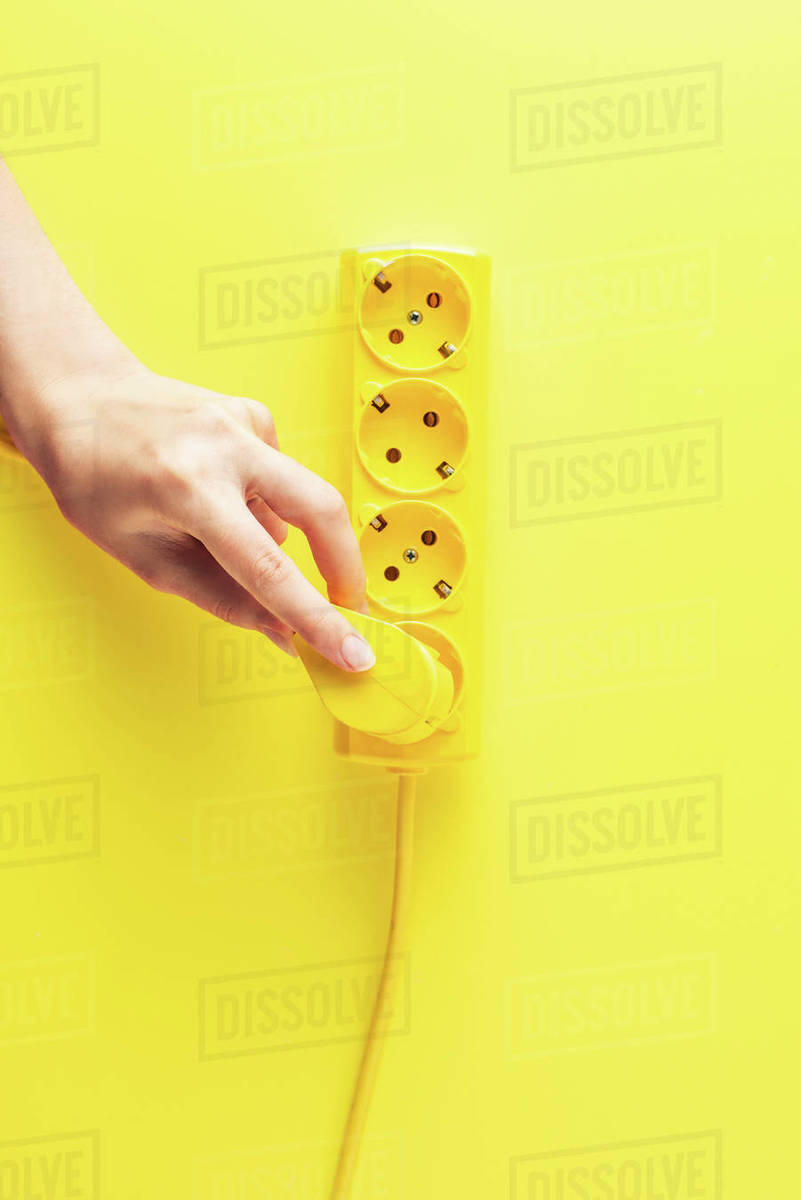 Cropped shot of person inserting plug into socket outlet on yellow ...