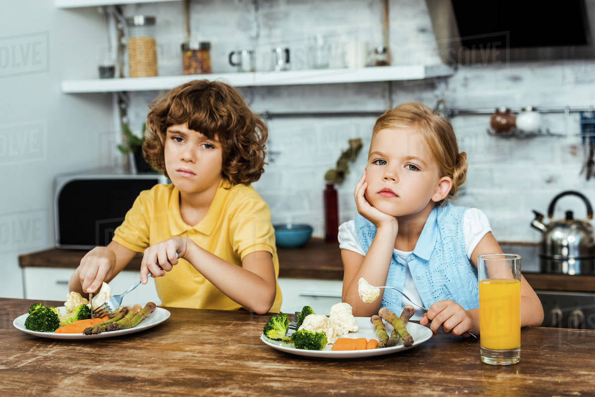 Bored children eating vegetables and looking at camera - Royalty-free ...