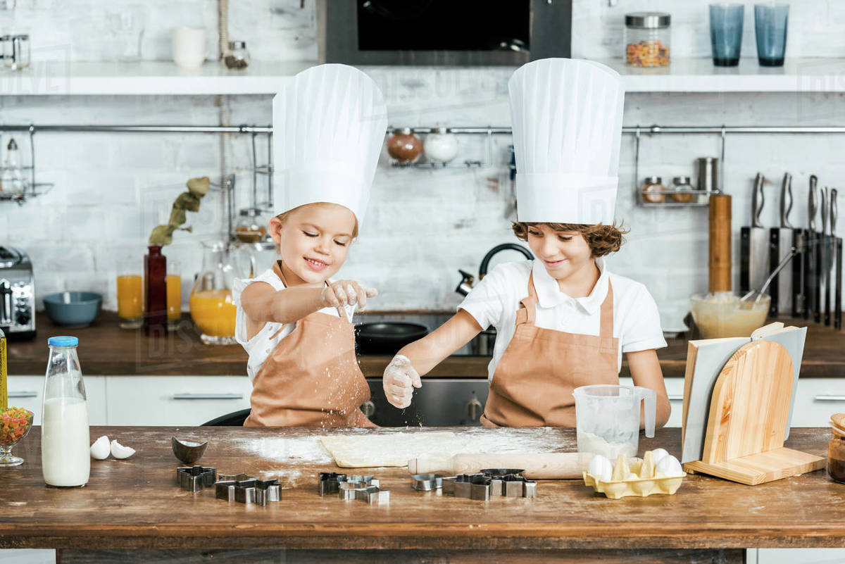 Cute happy children in aprons and chef hats preparing dough for tasty ...