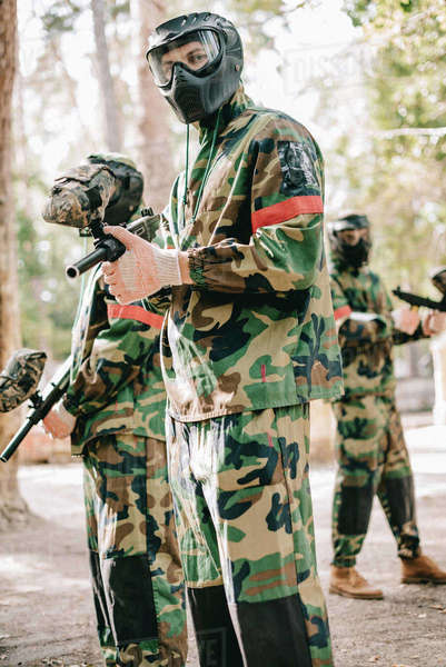 Male paintball player in uniform and goggle mask looking at camera and ...