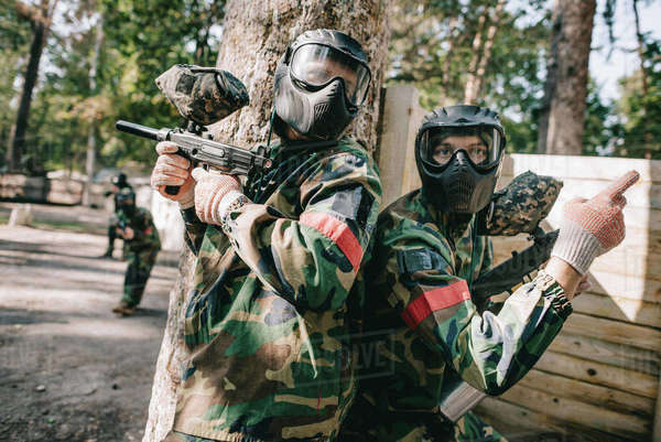 Male paintball player in camouflage and goggle mask pointing by finger ...