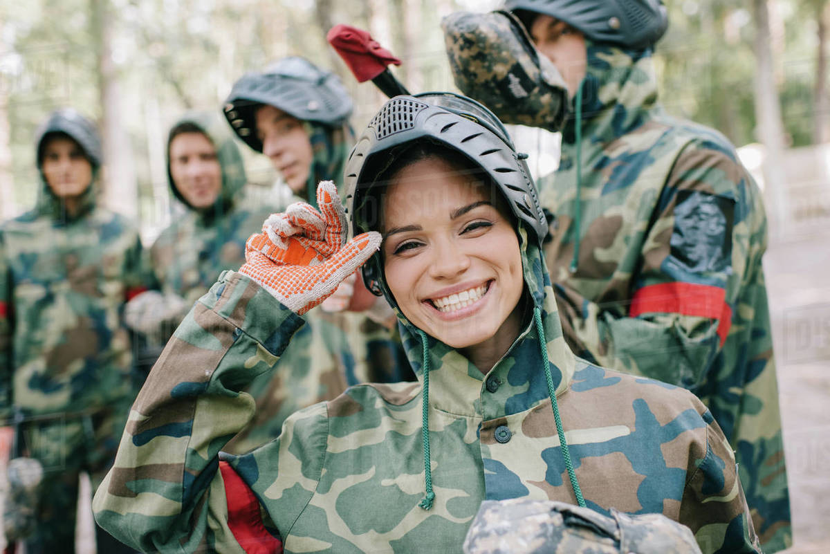 Portrait of laughing female paintballer in uniform looking at camera ...