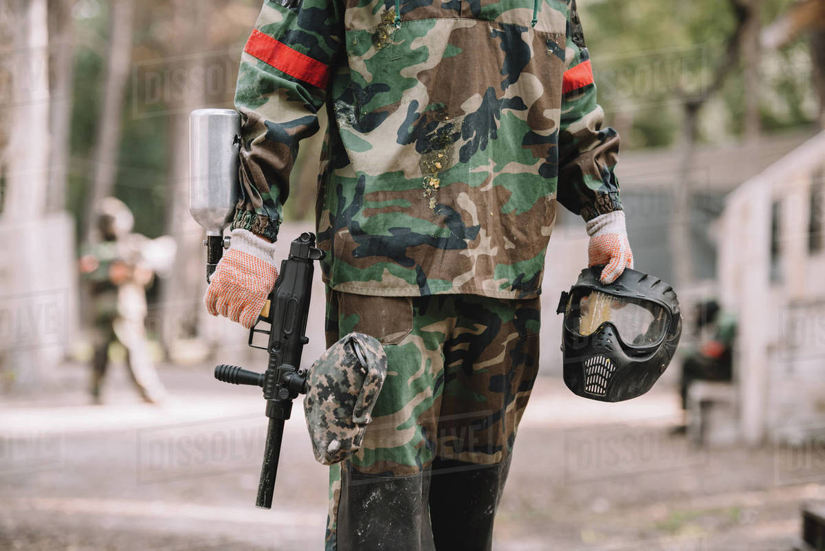 Cropped image of paintball player holding marker gun and goggle mask ...