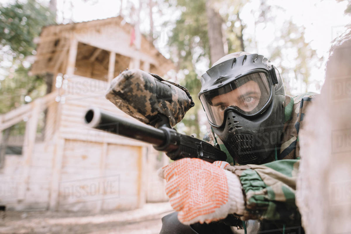 Serious male paintball player in goggle mask and camouflage aiming by ...