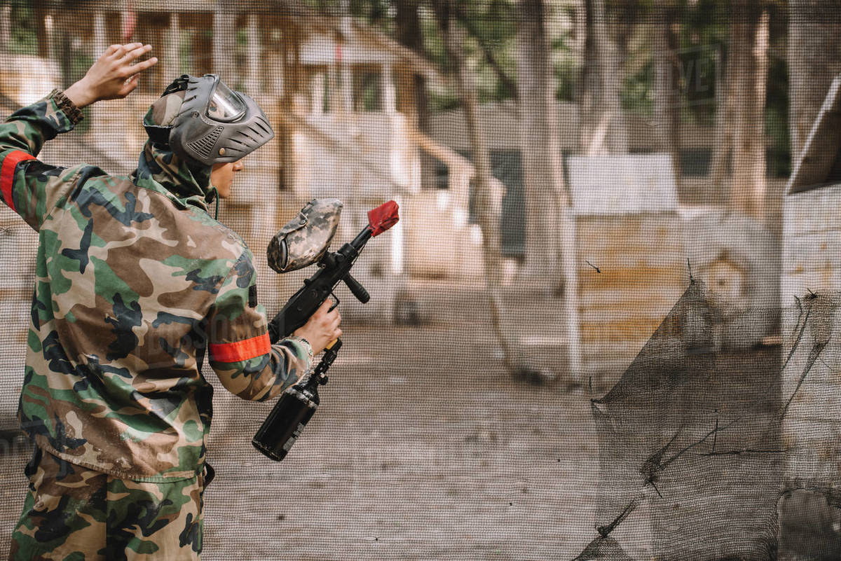 Rear view of male paintball player in goggle mask and camouflage with ...