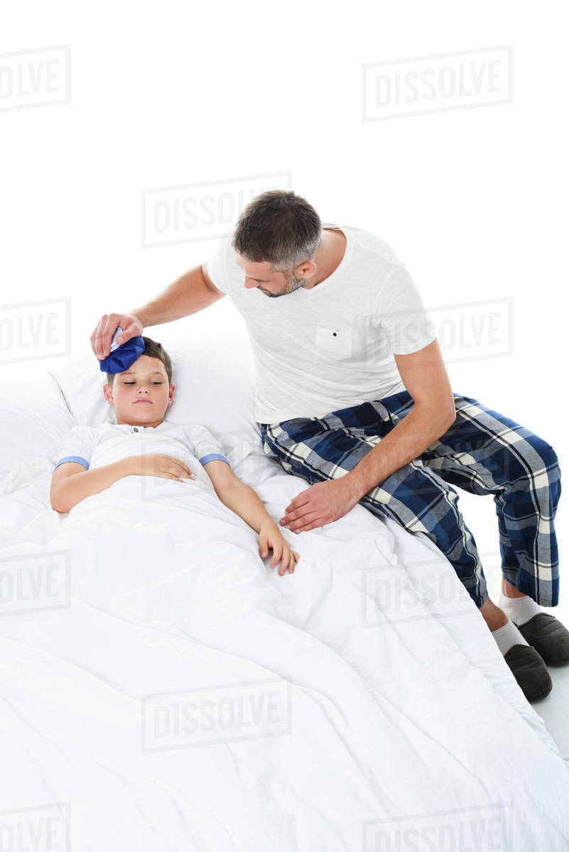 Father holding ice pack on head of sick son with temperature lying in ...