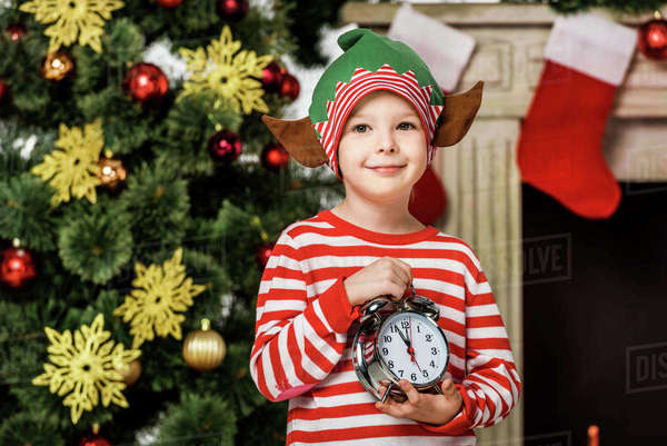 Adorable little kid in elf costume with alarm clock standing in front ...