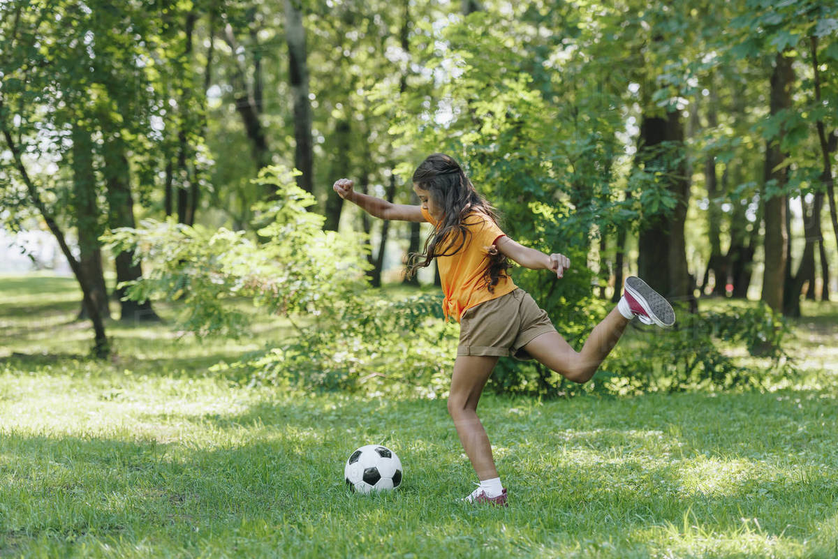 Side view of child kicking soccer ball in park - Stock Photo - Dissolve