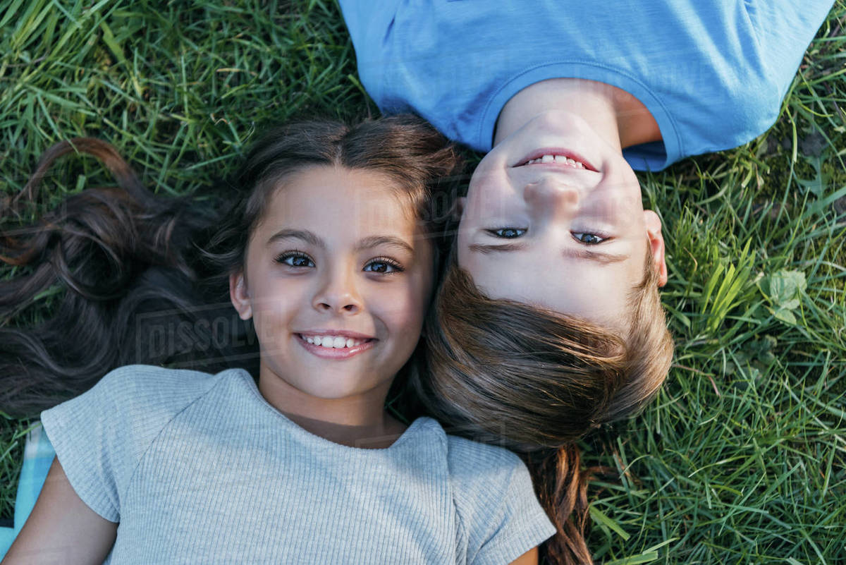 Top view of cute happy children lying on grass and smiling at camera ...