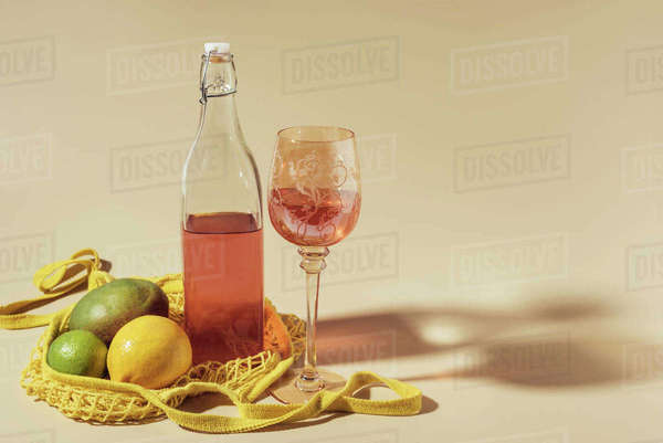 Close-up view of drink in glass and bottle, string bag and fresh fruits ...